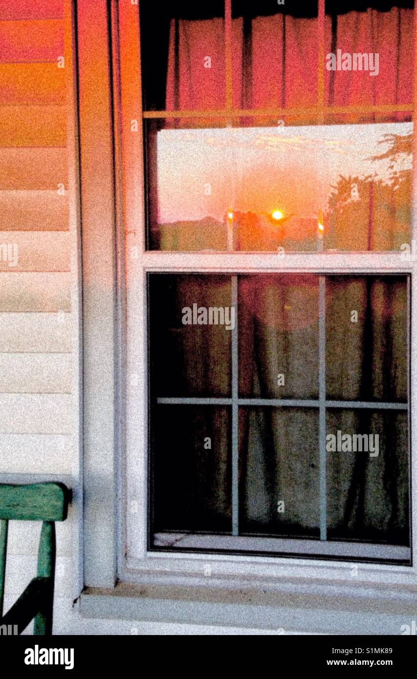 Coral sunset reflected in window with green bench Stock Photo - Alamy