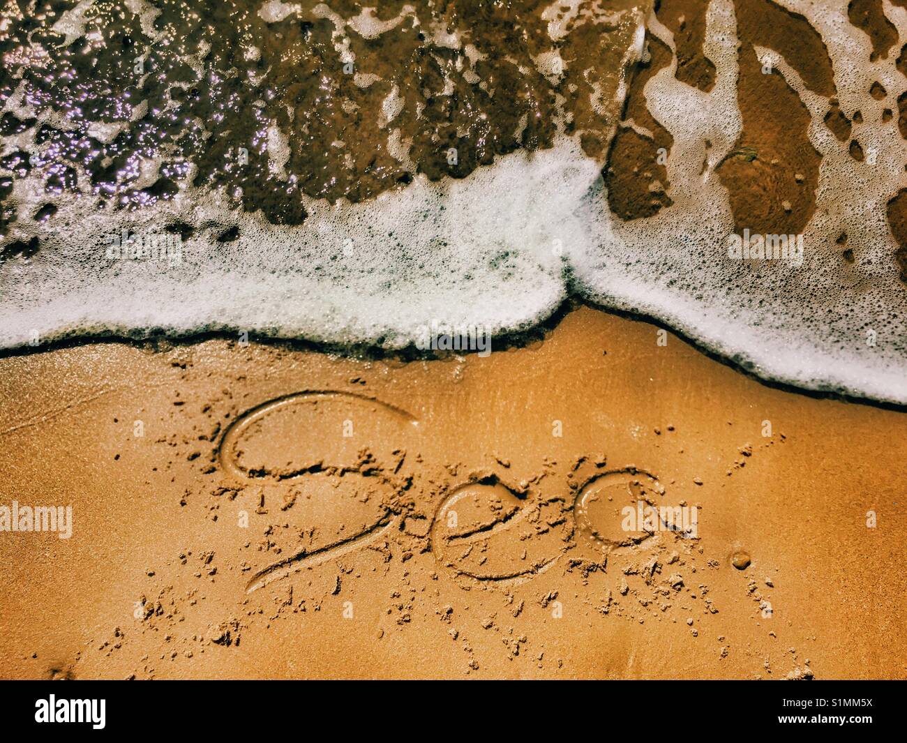 Tide coming in to erase sea written in the sand Stock Photo - Alamy