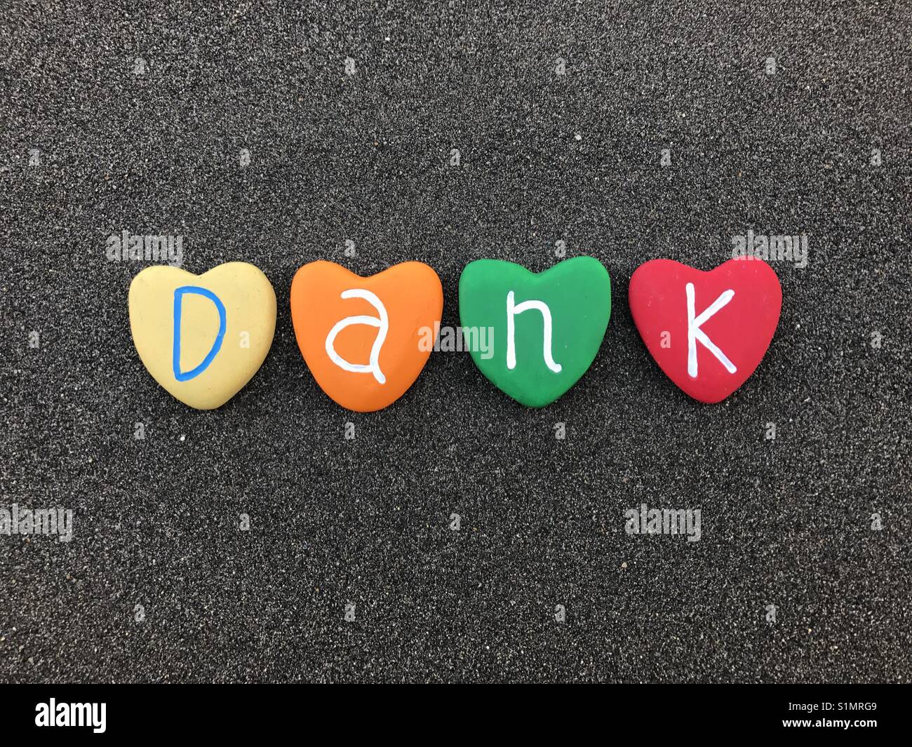 Dank, danish thank you with colored heart stones over black volcanic ...
