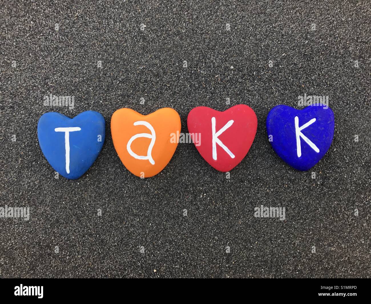 Takk, norwegian thank you with colored heart stones over black volcanic ...