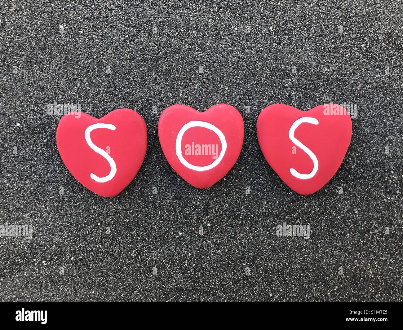 SOS with red colored heart stones over black volcanic sand Stock Photo ...