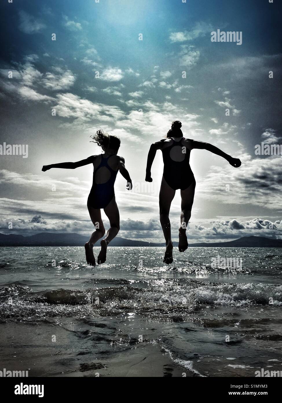 Two children having fun jumping over waves backlit by the sun at ...