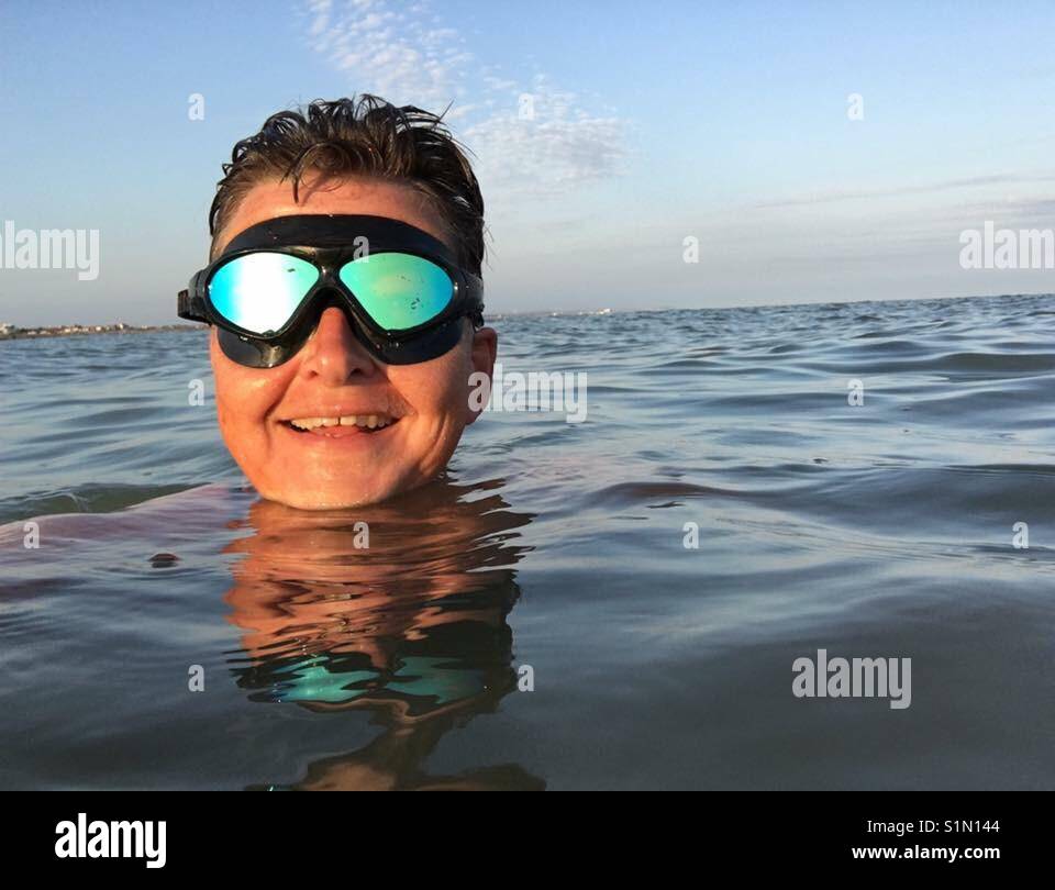Lady with mirrored swim giggles and her reflection swimming in the sea ...