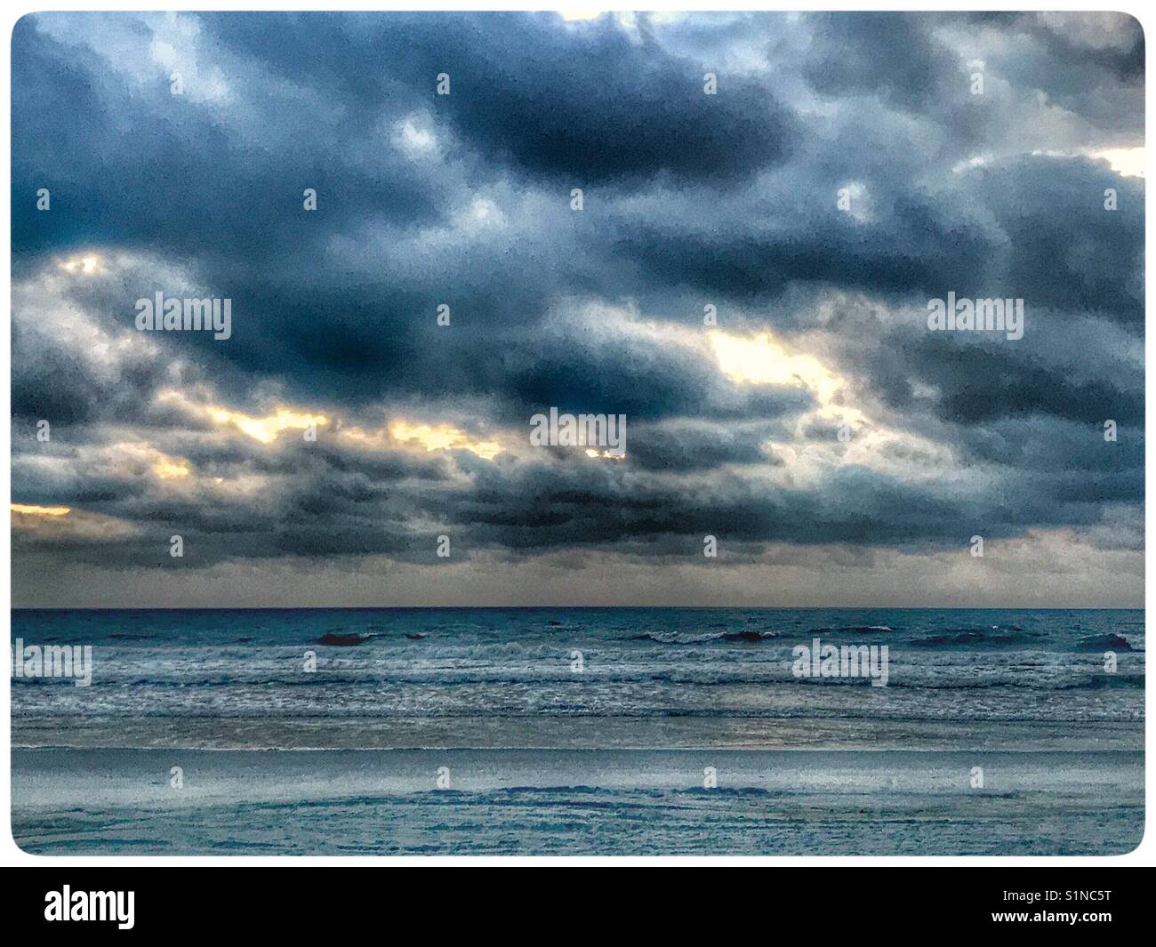 Sunrise storm clouds stir over a calm ocean shoreline Stock Photo - Alamy