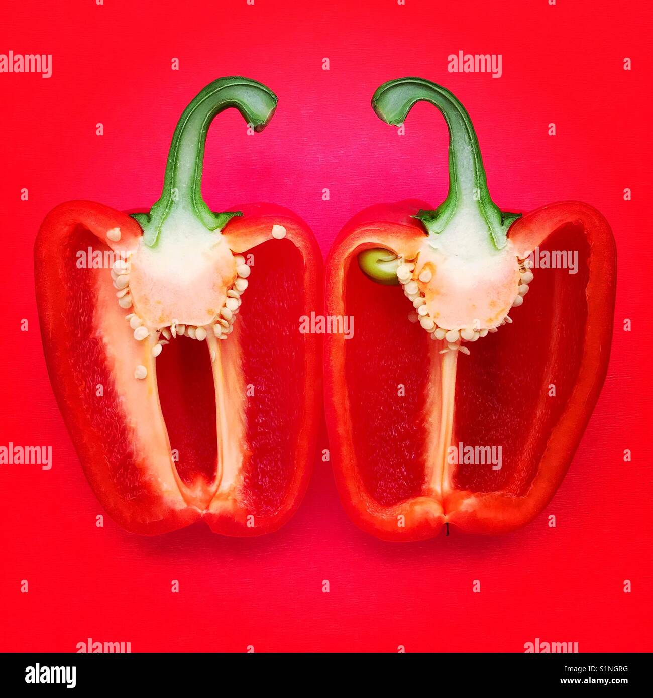 An overhead detail shot of a whole red pepper cut in half on a red ...