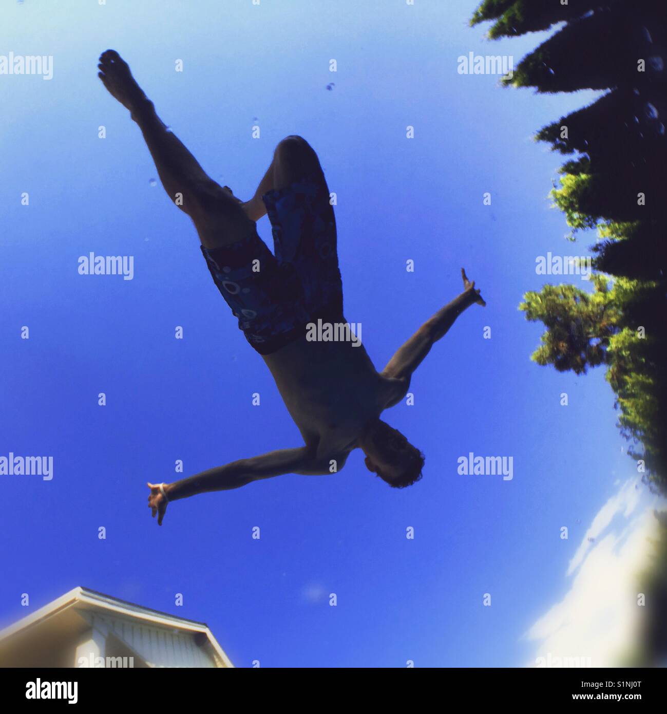 Teenage boy flying through the air from a diving board into a swimming ...