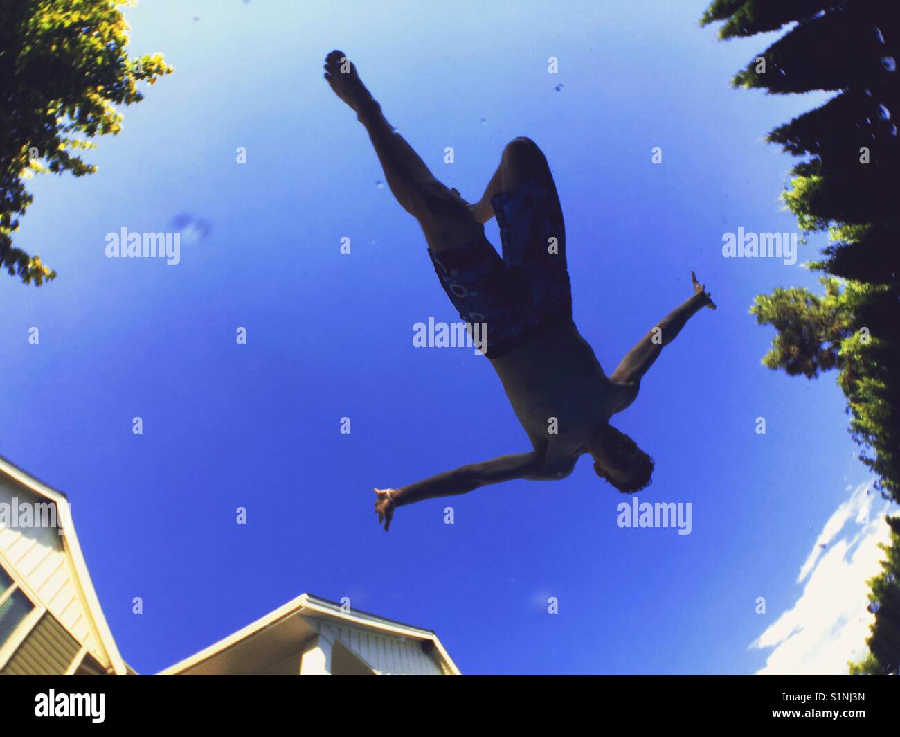 Looking up at a young man flying through the air off a diving board ...