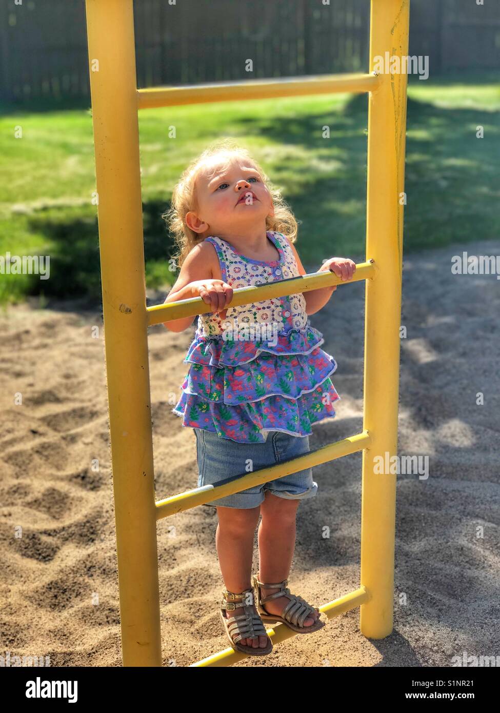 Baby climbing the ladder on the playground equipment while looking up ...