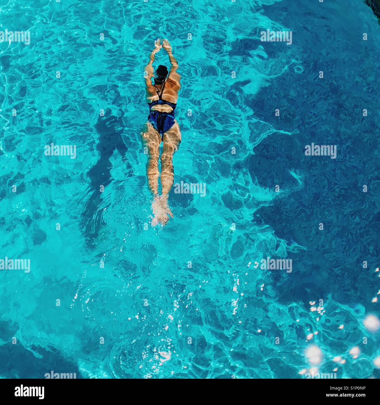 Woman in swimming face down in outdoor swimming pool on a sunny day ...