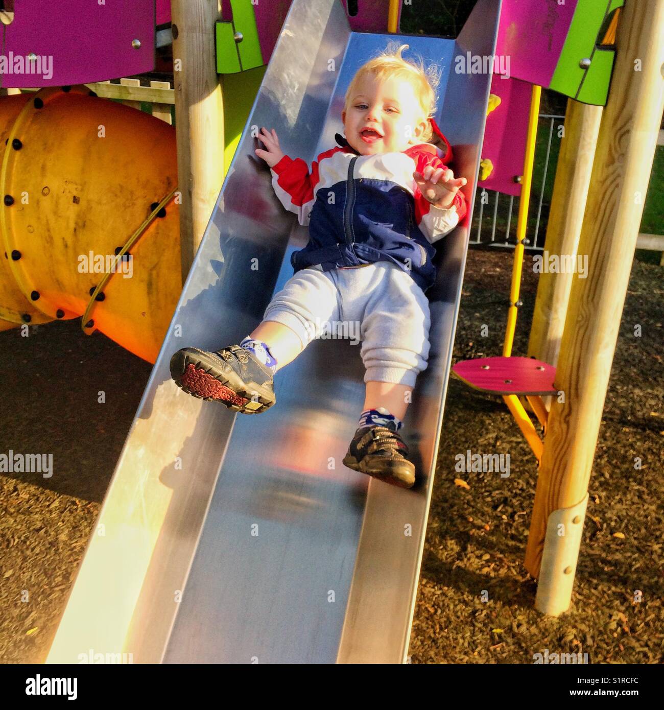 One year old baby boy on a playground slide, Hampshire, England, United ...