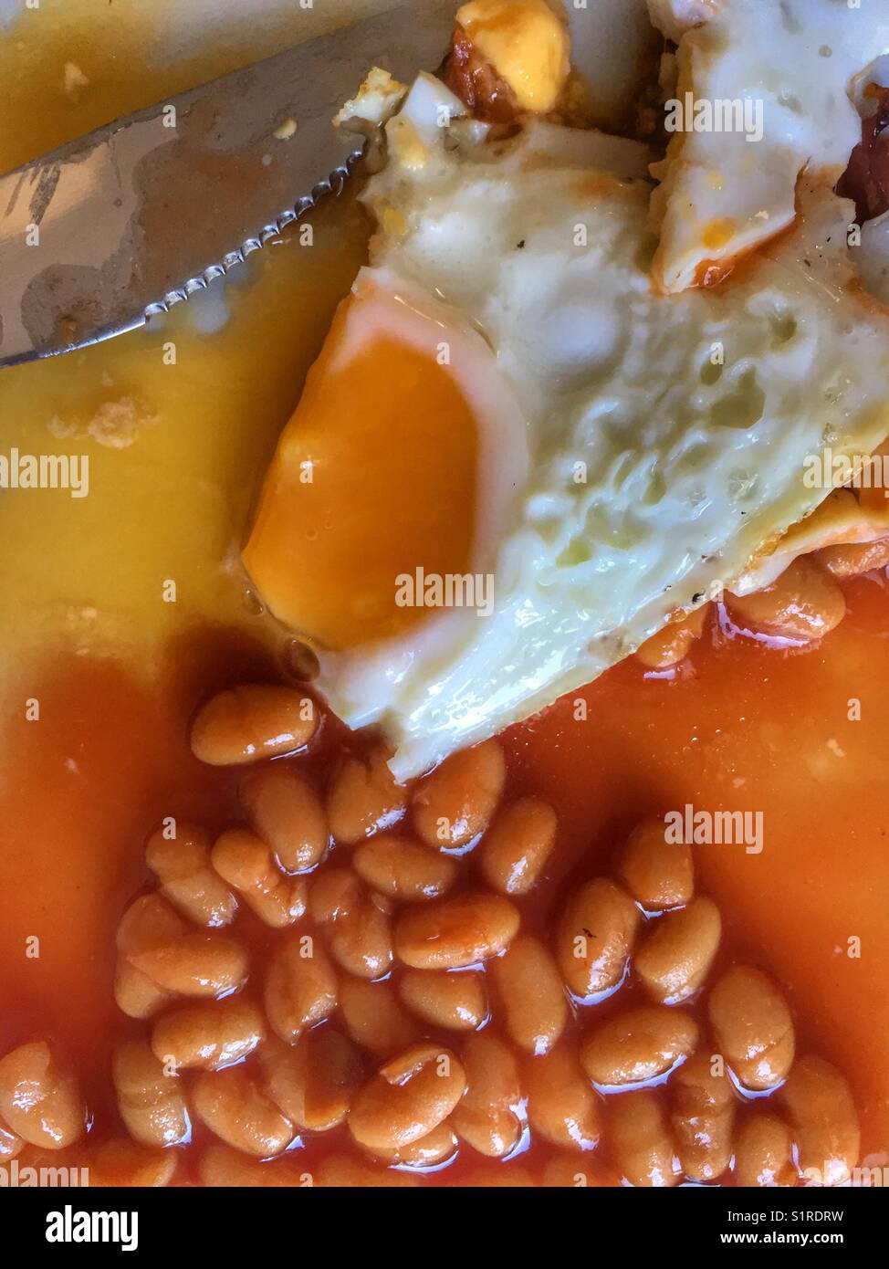 A partially eaten breakfast of a fried egg and baked beans Stock Photo ...