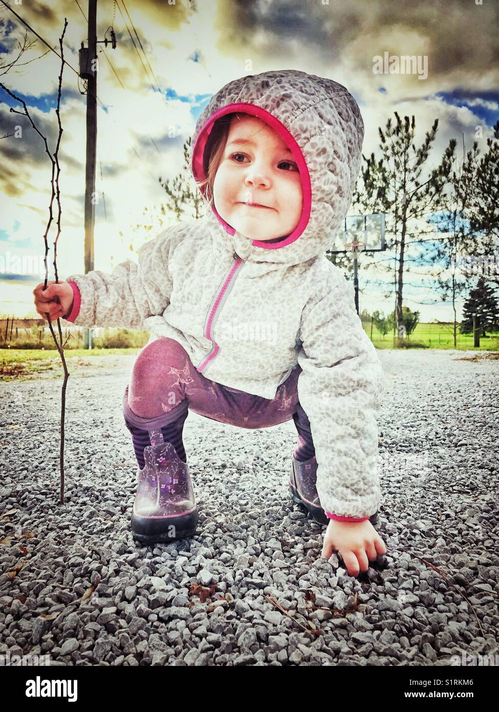 Toddler girl playing with rocks and holding stick outside Stock Photo ...