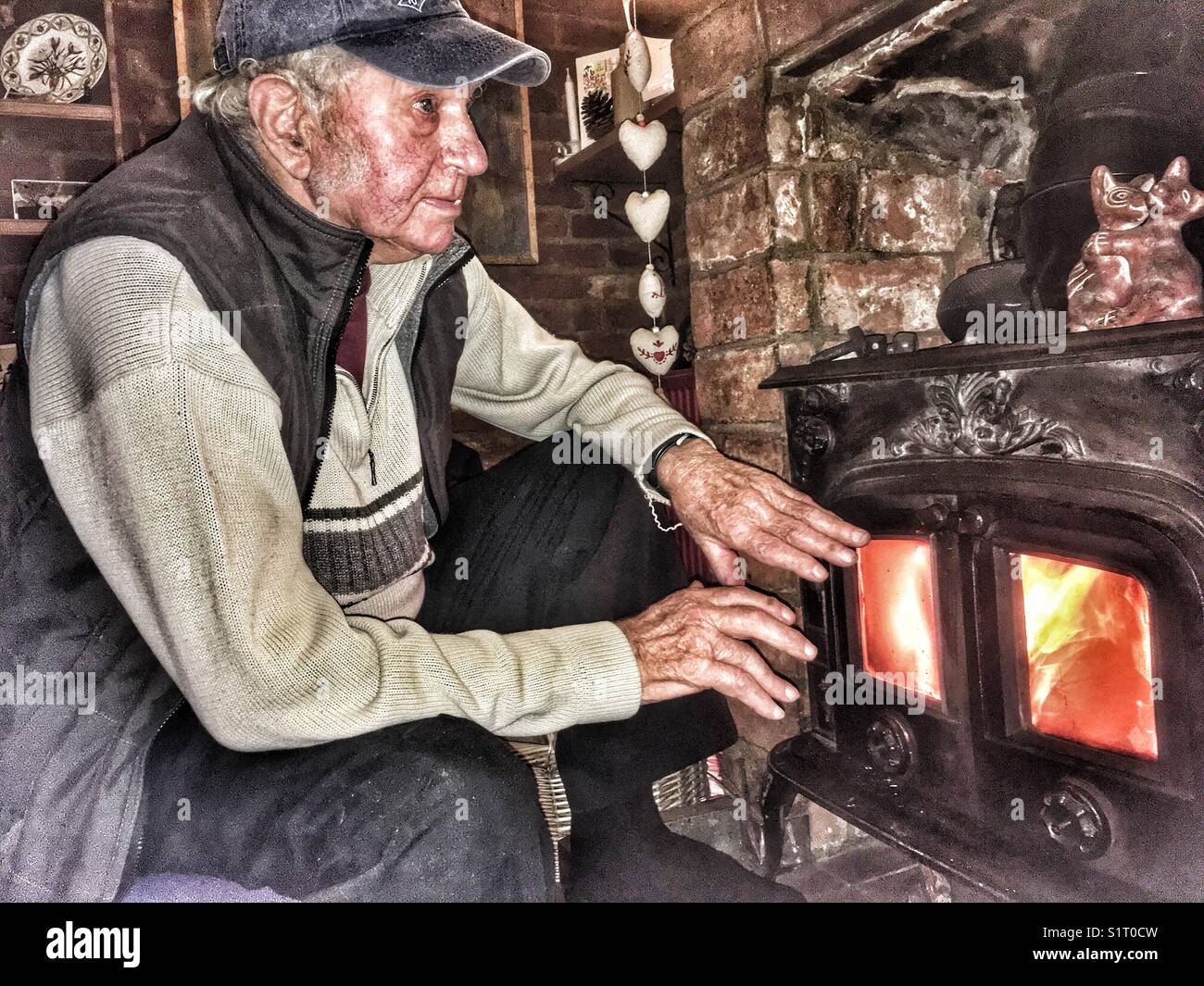 Old age pensioner keeping warm beside a wood burning fire in his ...