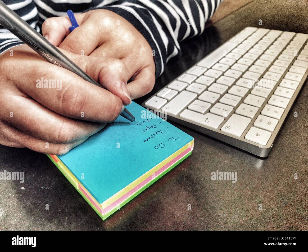 Millennial writing a list on a sticky notepad, at a desk, next to s ...