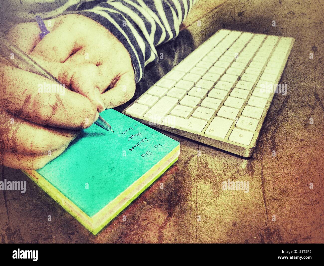 Millennial writing a list on a sticky notepad, at a desk, next to a ...