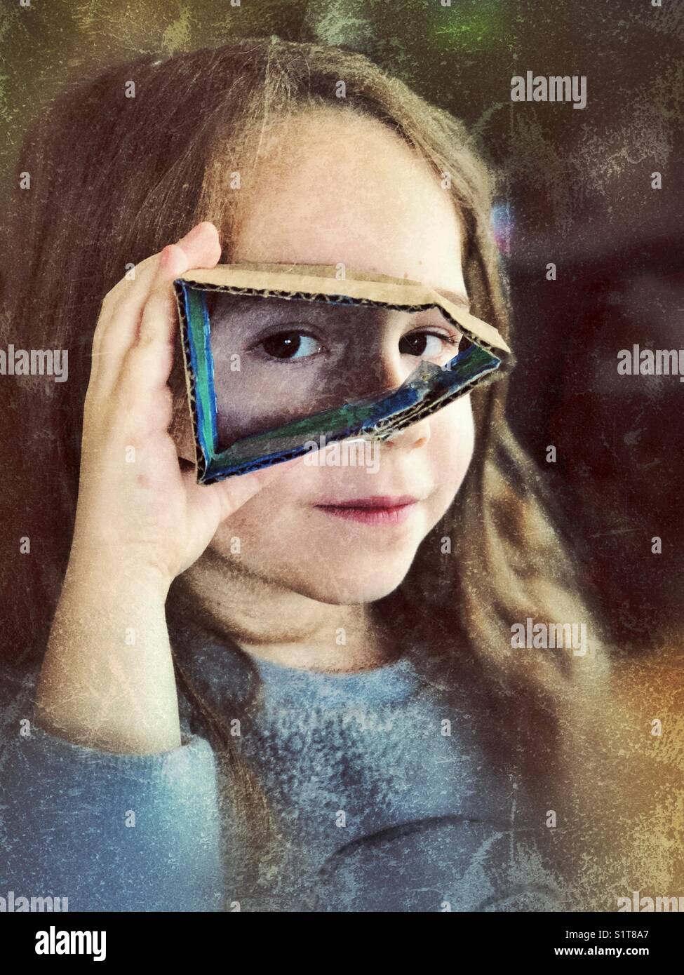 Portrait of a young girl looking through a piece of cardboard shaped ...