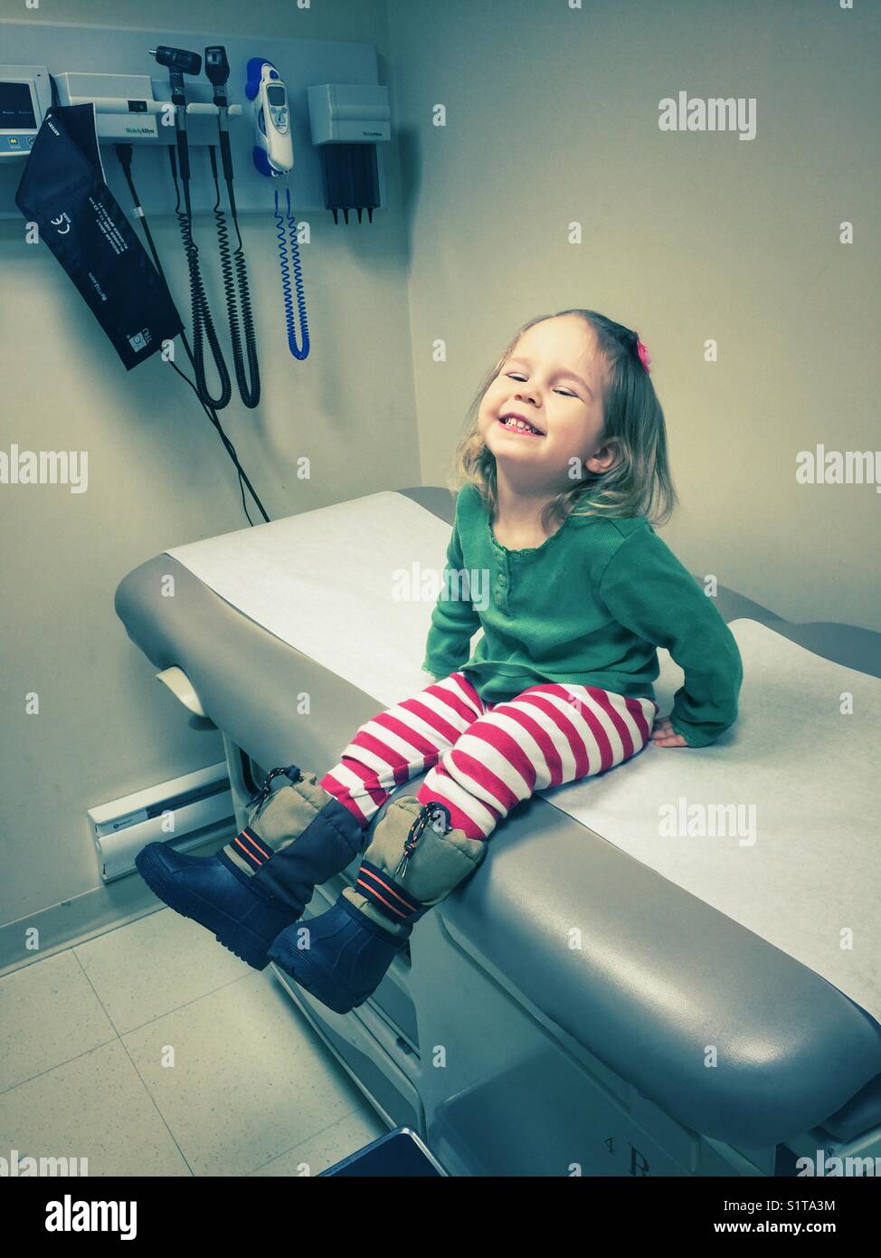 Young girl sitting on an examination table in a doctor’s office smiling ...