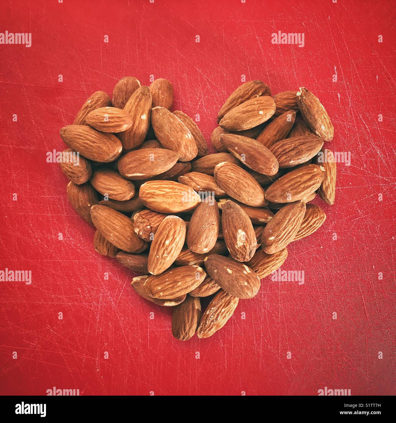 Raw whole shelled almonds in the shape of a heart on a red cutting ...