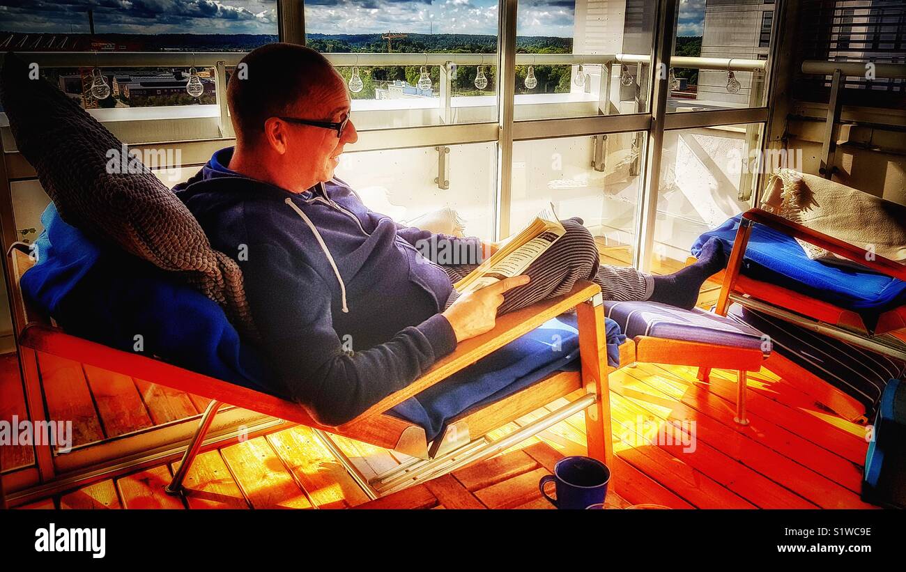 Middle aged Caucasian man lying on reclining chair on enclosed terrace ...