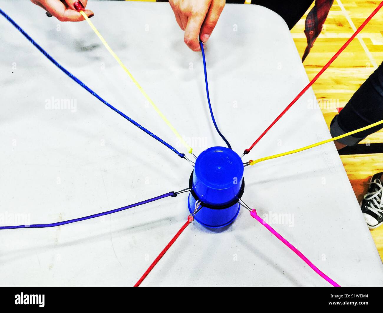 Hands working together trying to move blue cup using colorful strings ...