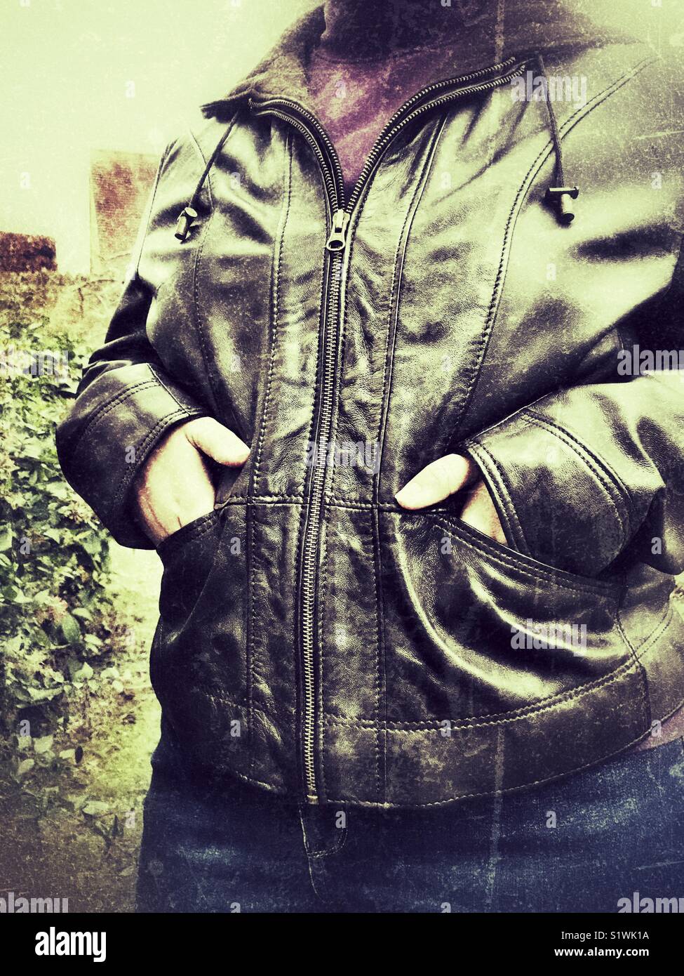Woman wearing a brown leather jacket, hands in pockets, midsection ...