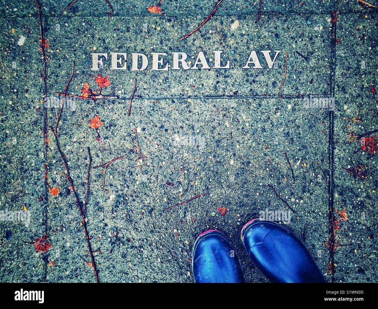 Feet in blue rain boots standing on a sidewalk with Federal Av metal ...
