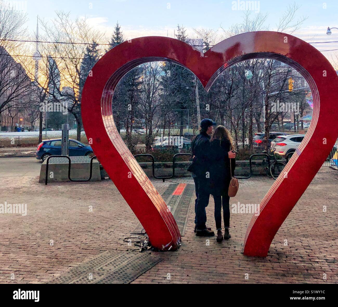 A couple stands under a large red heart sculpture in Toronto Stock ...