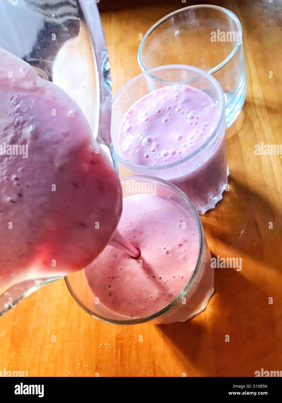 Pouring a strawberry smoothie from blender into glasses, for a healthy ...