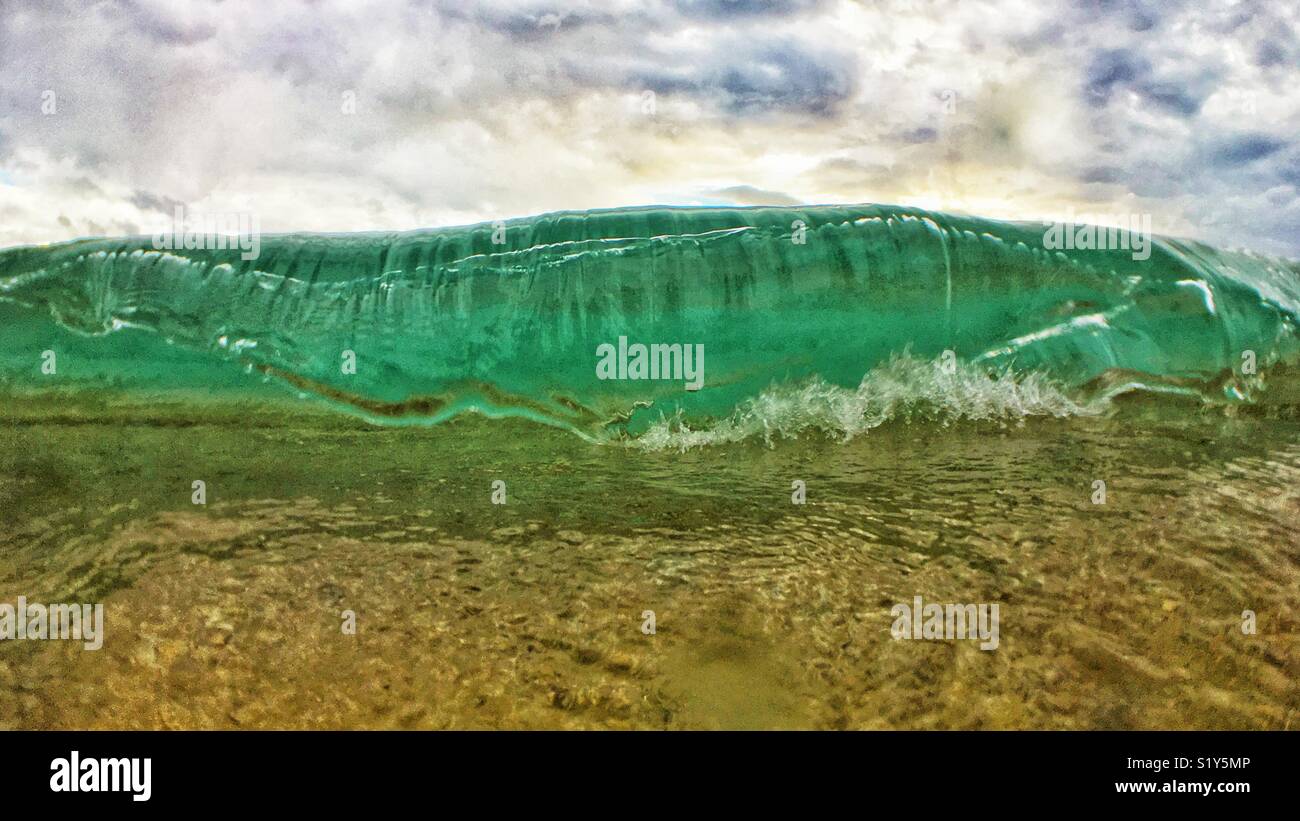 Turquoise ocean wave crashing over a sandy beach with a partially ...
