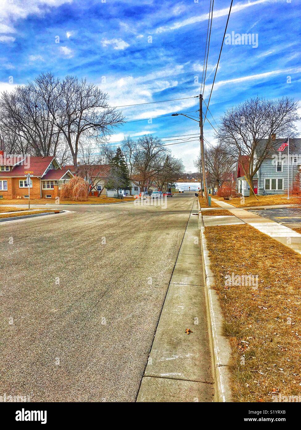 Suburban road leading towards a lake with power lines and vivid sky ...