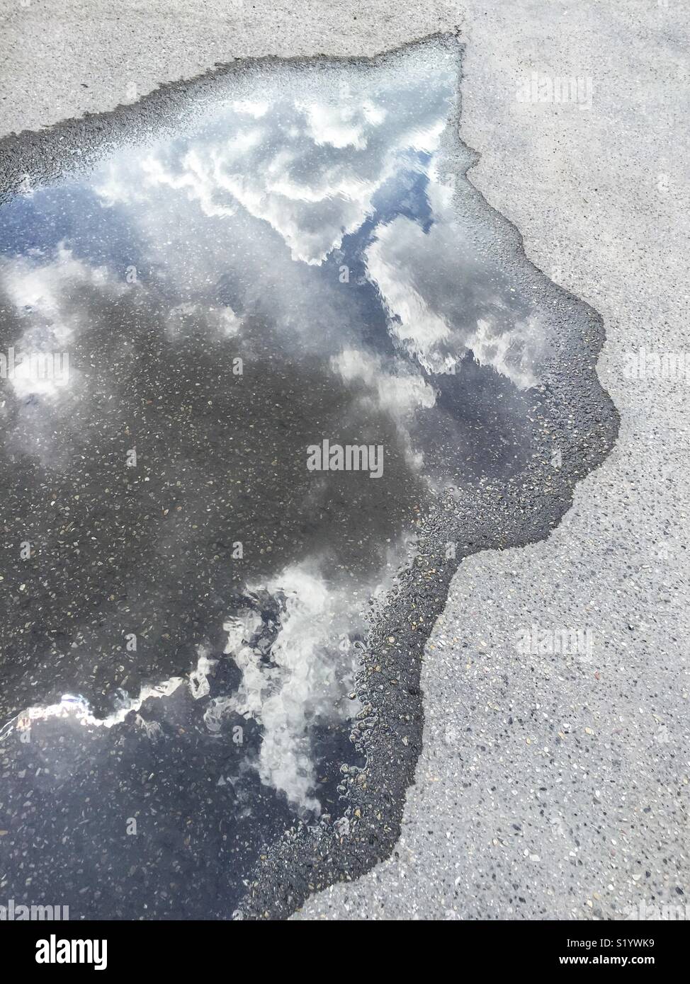 Clouds are reflected in a puddle on pavement Stock Photo - Alamy