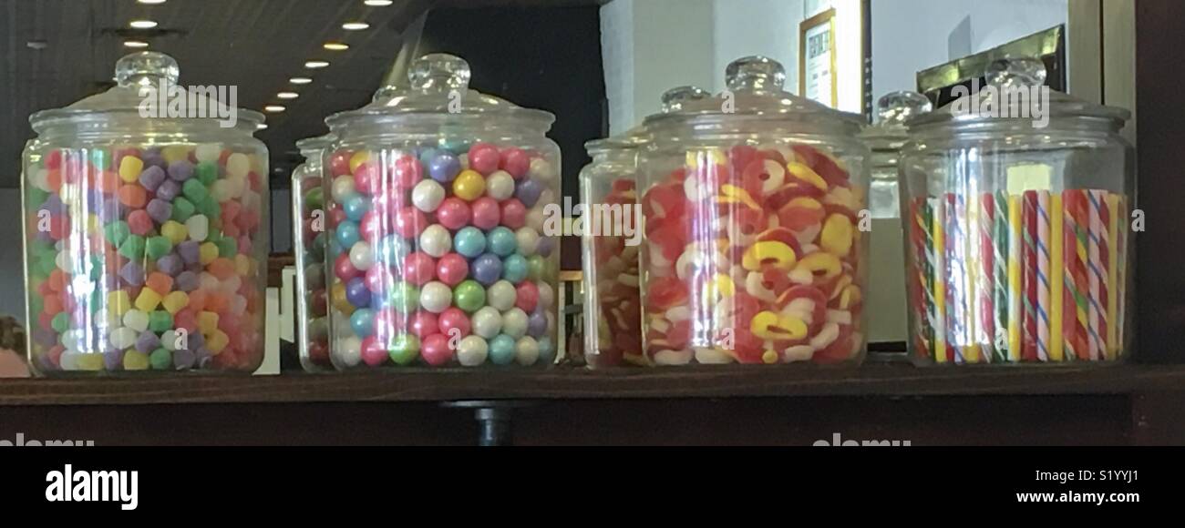 Four glasses jars filled with various candies on display for all to see ...