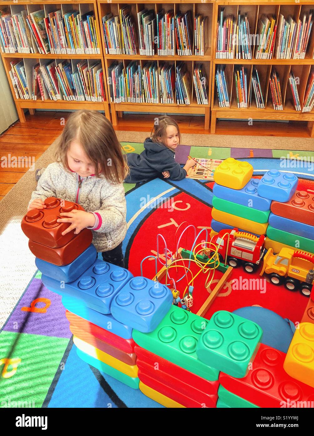 Two young girls playing with toys on colourful alphabet carpet in ...