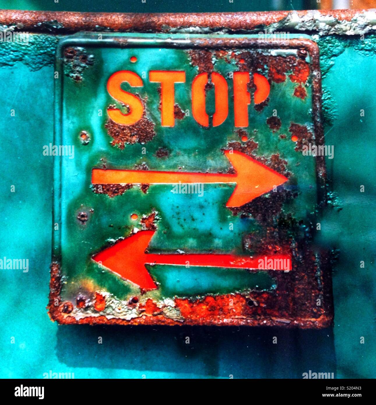 Rusted sign with writing stop and directional arrows in both directions ...
