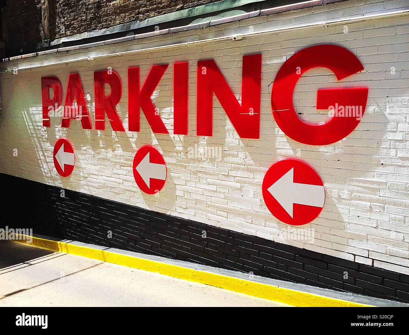 Oversized red parking and arrows signage on a whitewashed brick wall to ...