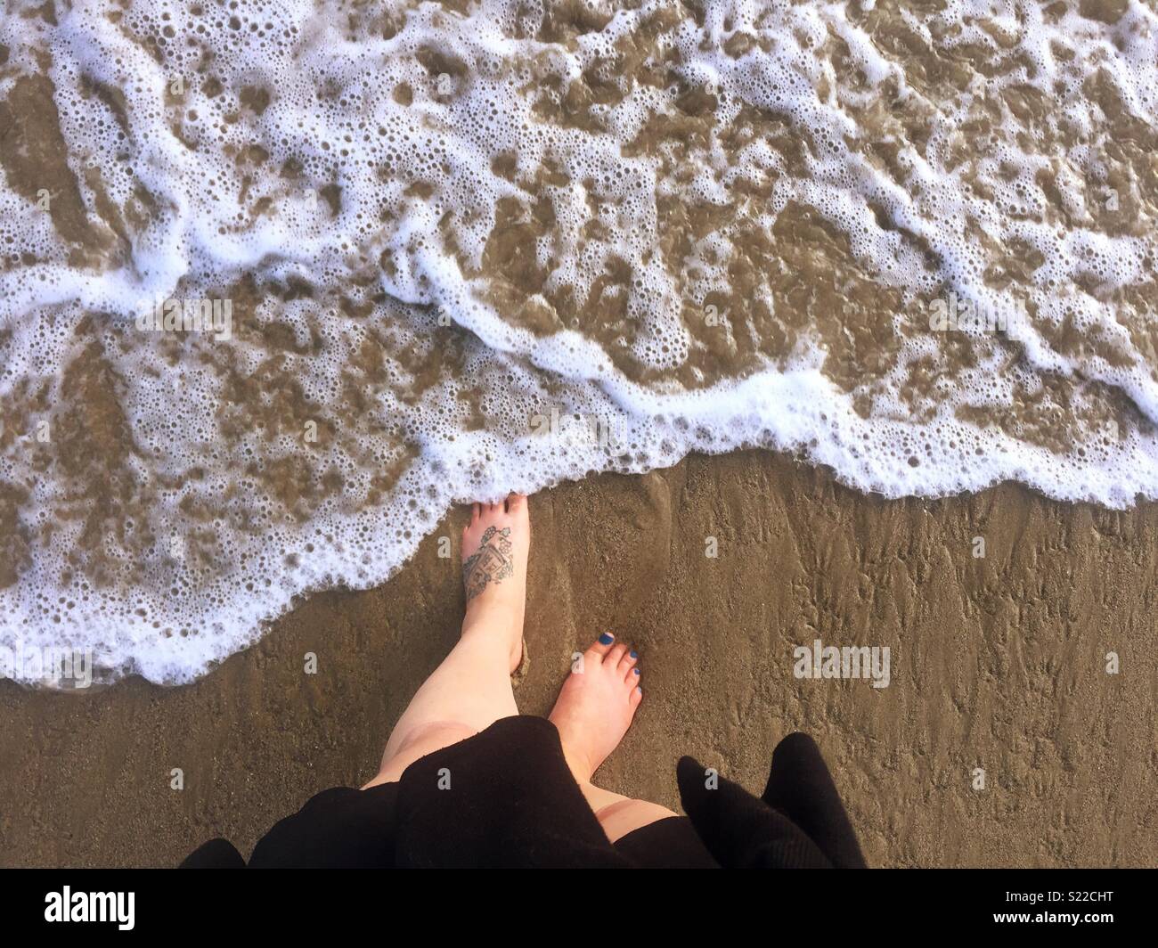 Woman on the beach wave hitting her feet Stock Photo - Alamy