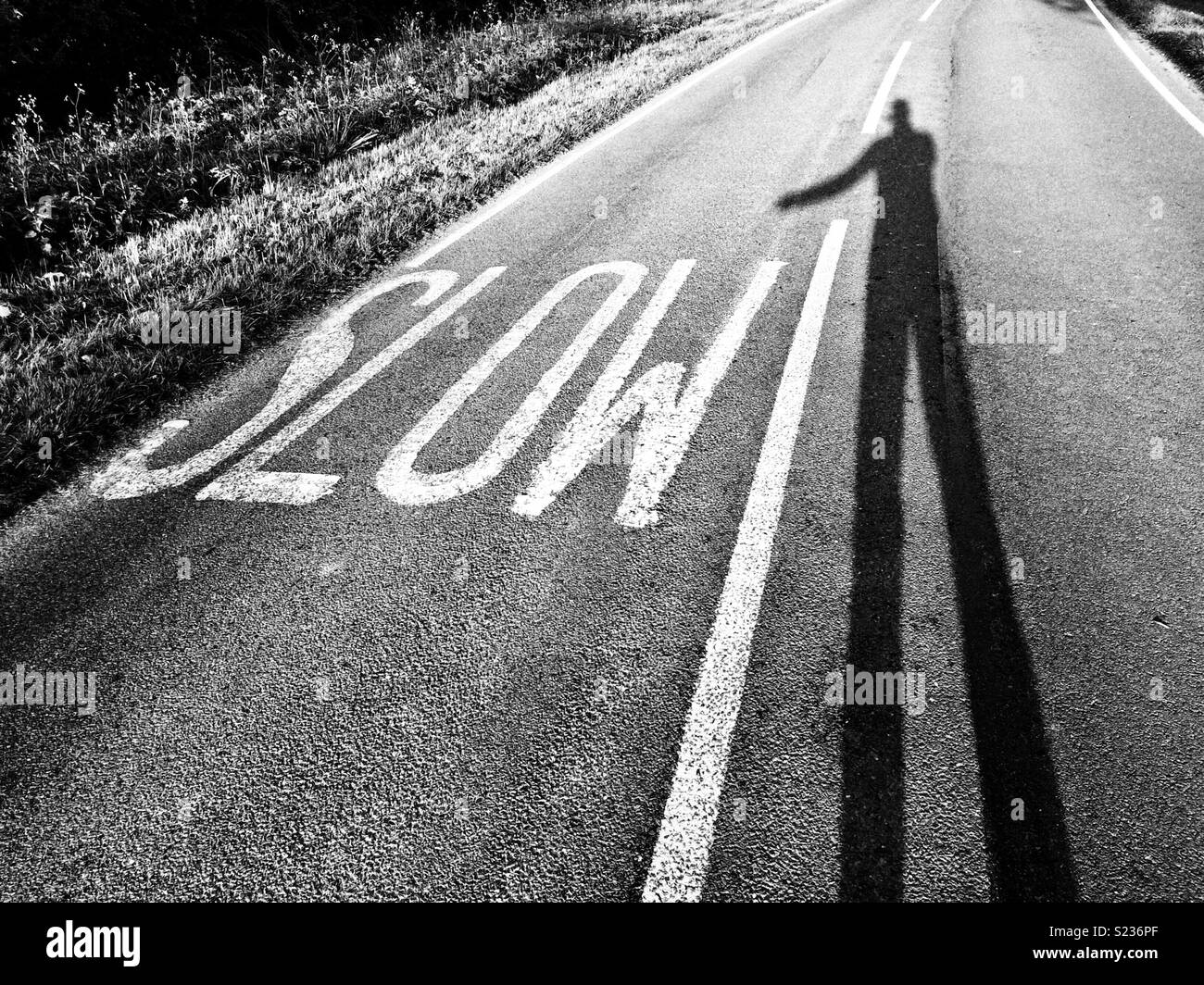 Human shadow pointing at a slow road marking on a rural road, UK Stock ...