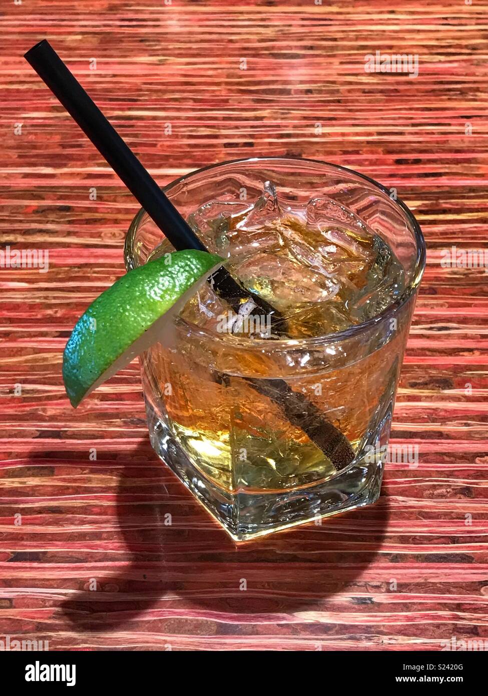 Refreshing iced mixer drink with straw and slice of lime, on a stripey ...