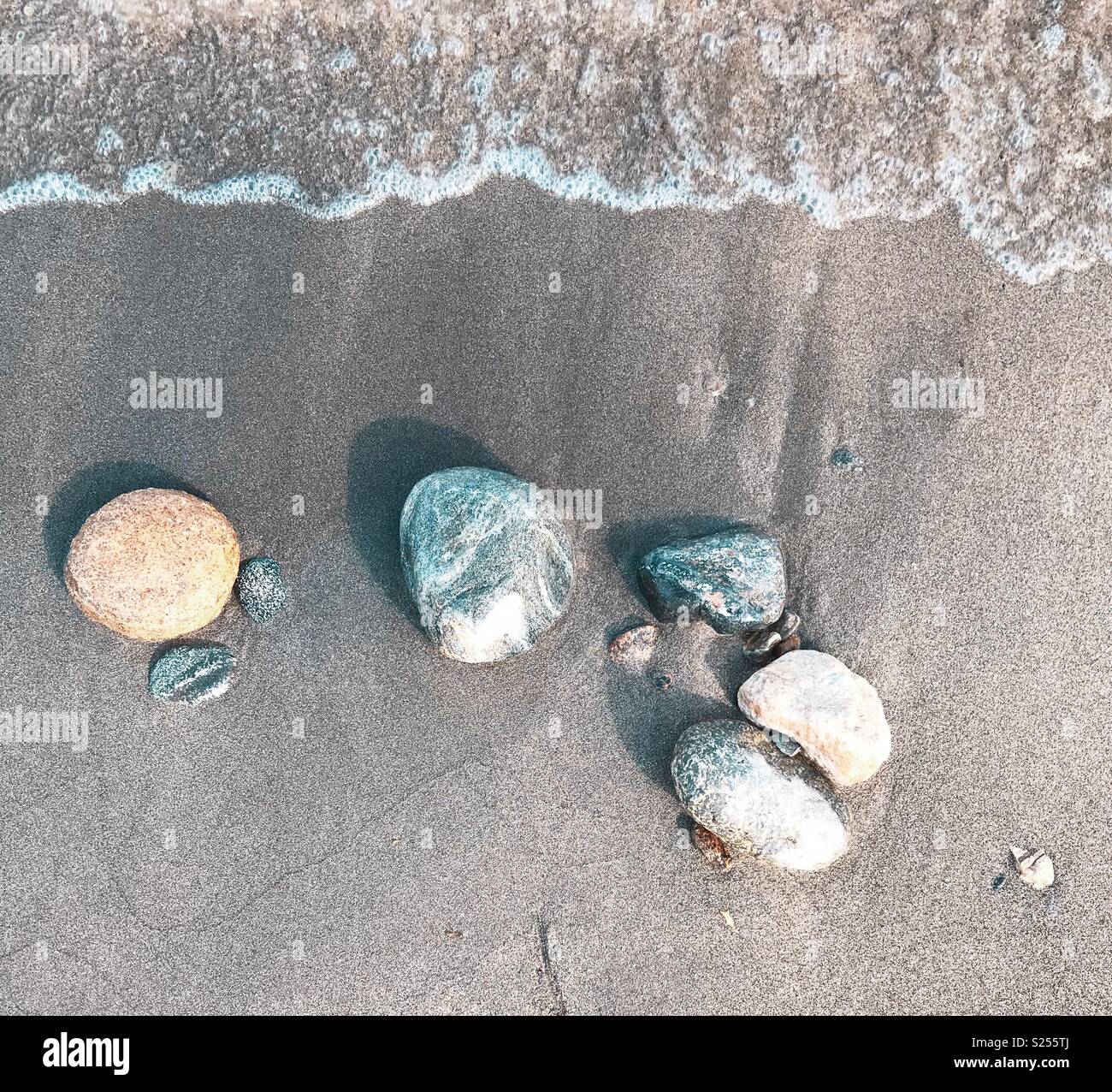 Stones and sticks on sand on the edge of Lake Maggiore, Italy, with the ...