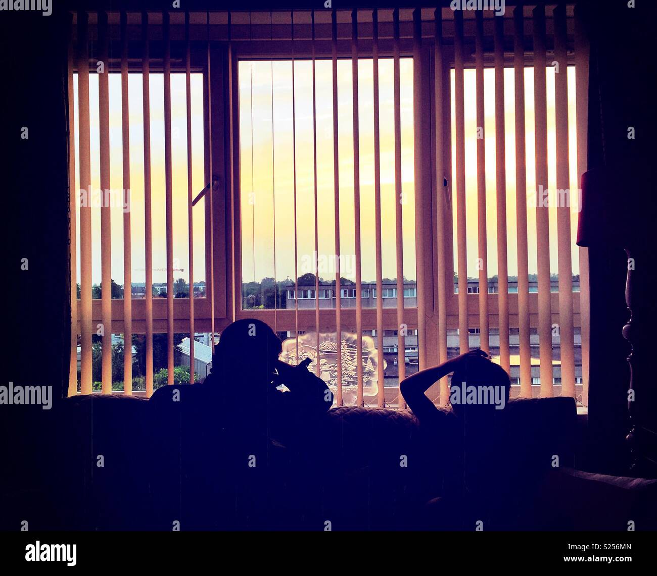 People in silhouette sat on a sofa in front of a window at sunset Stock ...