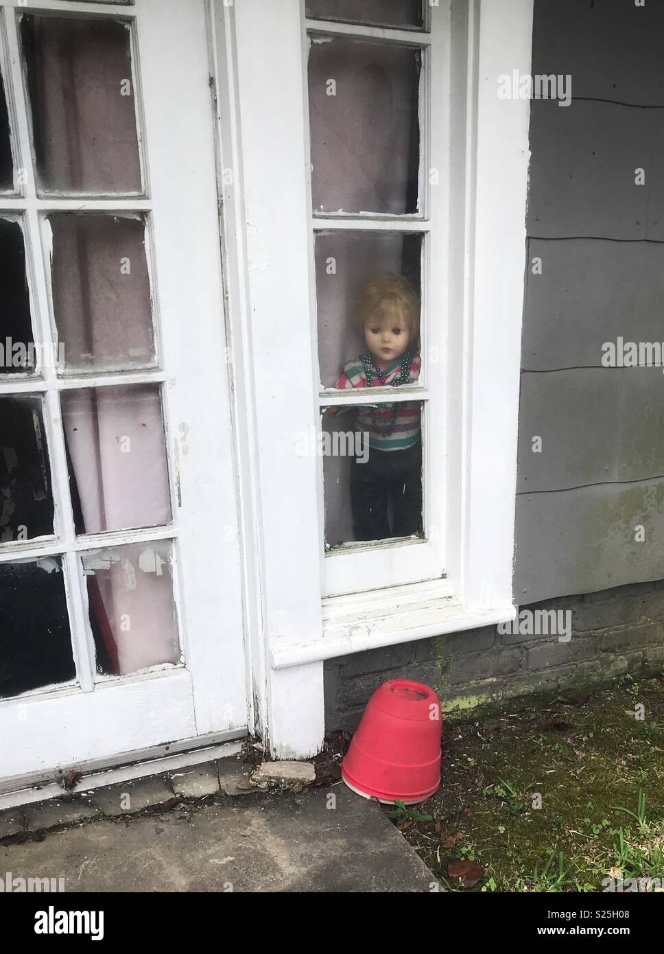 Creepy doll looking out of house window Stock Photo - Alamy