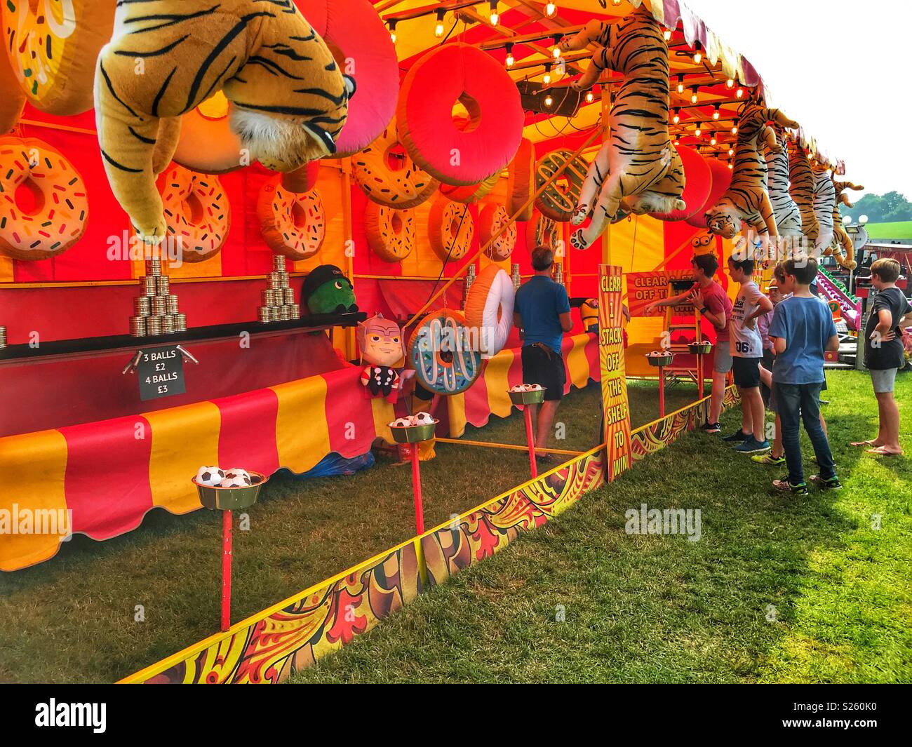 Group of young boys throwing balls at a coconut shy style of side stall ...
