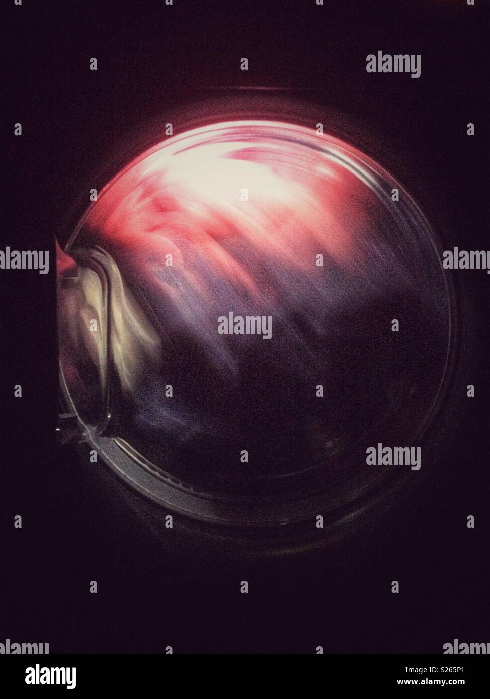 Clothes spinning in a dryer in a dark room with the light on Stock ...