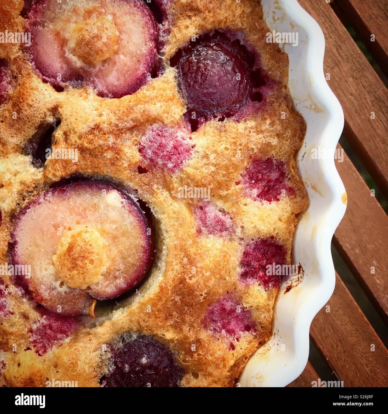 Plum and raspberry sponge cake in quiche dish outside on picnic table ...