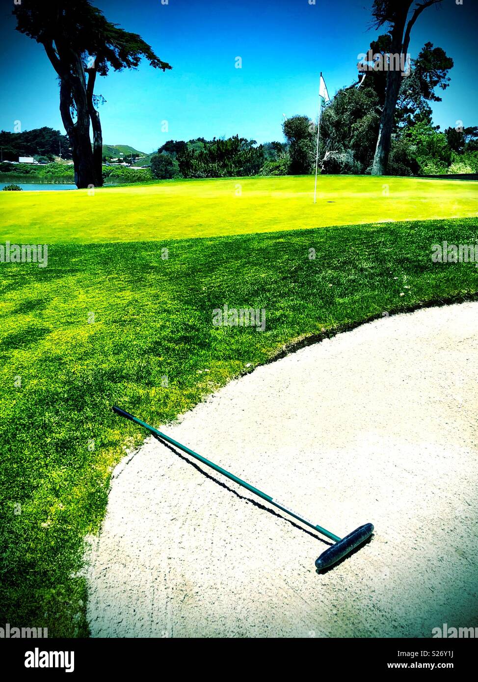 Bunker rake in sand trap with golfing green and lake in the background ...