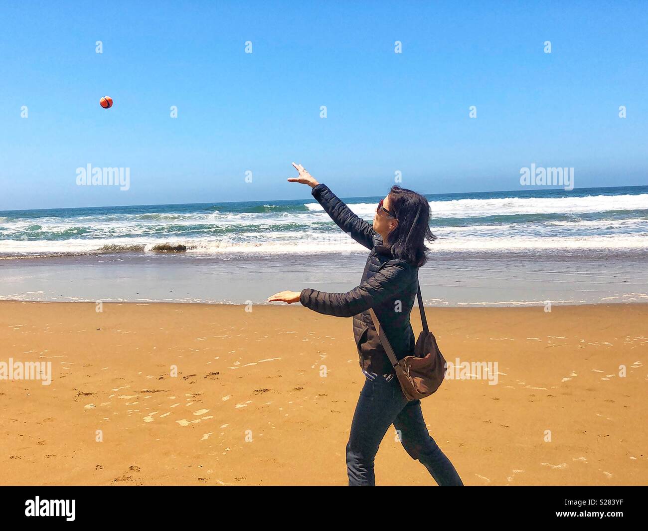 Young brunette woman throwing orange ball at a golden sand beach at ...