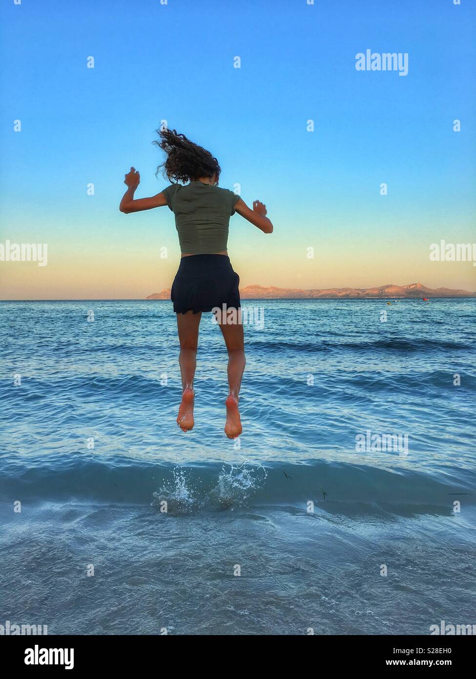 Young girl jumping in sea at dusk Stock Photo - Alamy