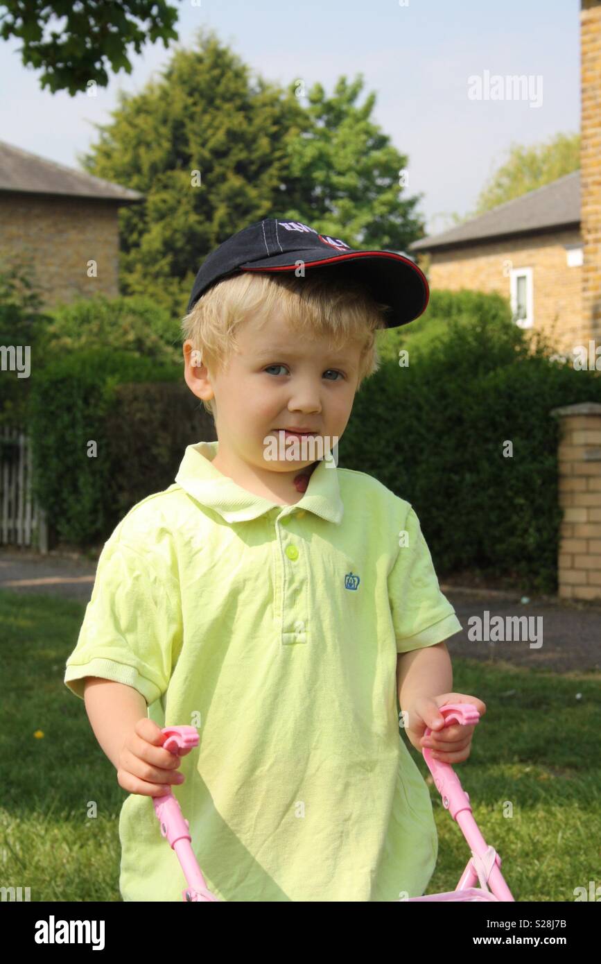 Young boy pushing a baby buggy on grass wearing a cap Stock Photo - Alamy