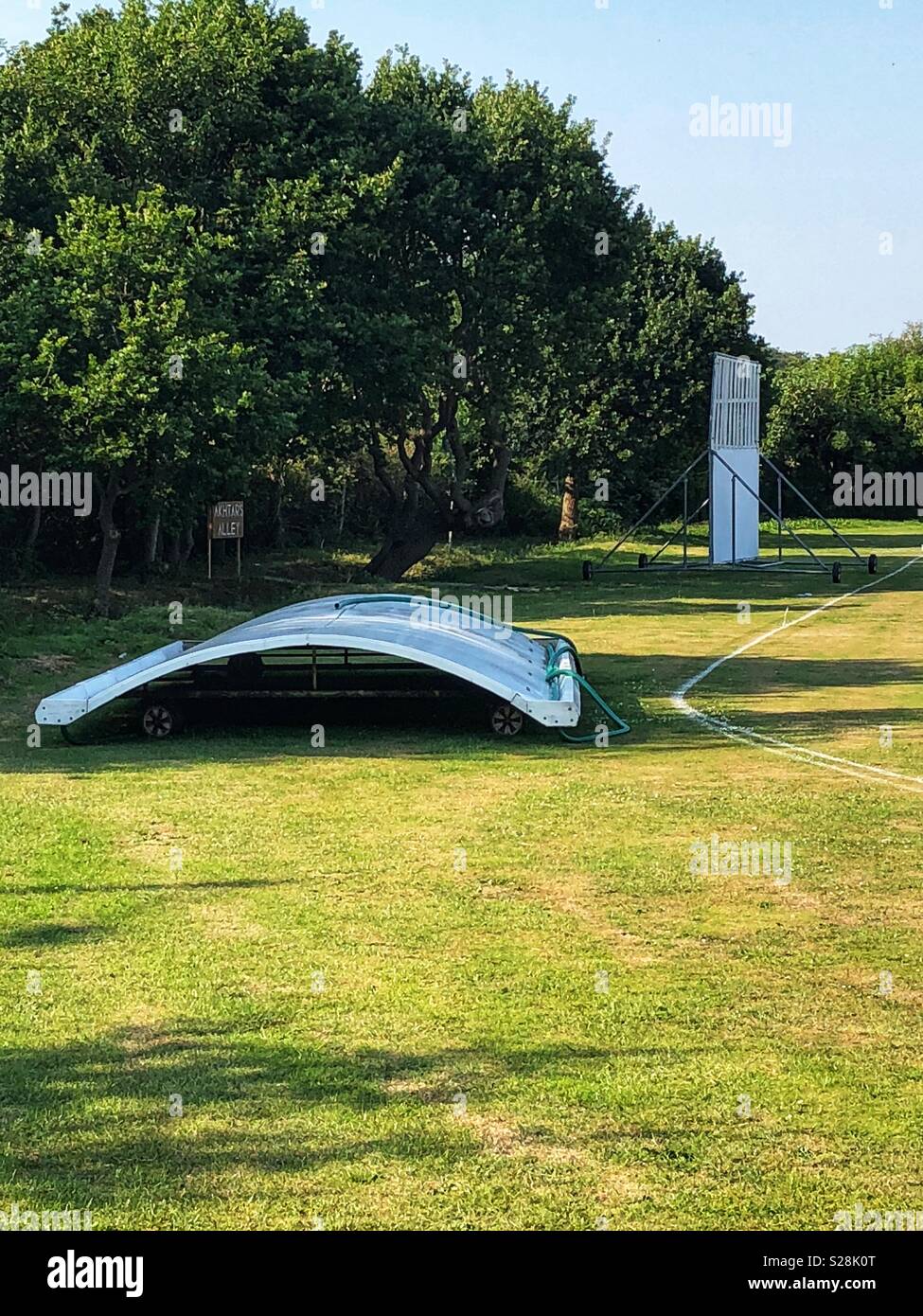 A cricket pitch cover and white sight-screen on wheels on the edge of a ...