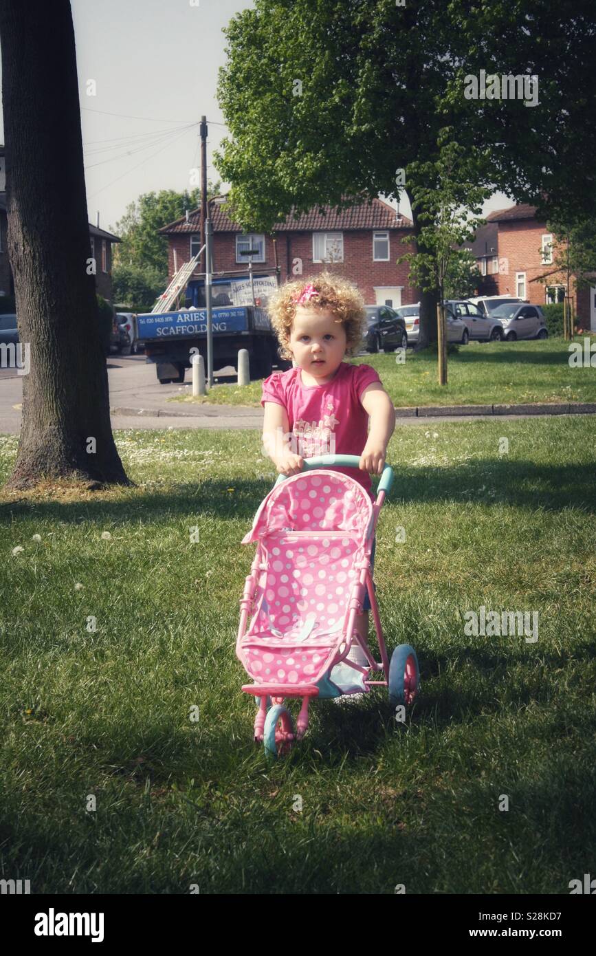 Little girl pushing pink dolls buggy on grass Stock Photo - Alamy